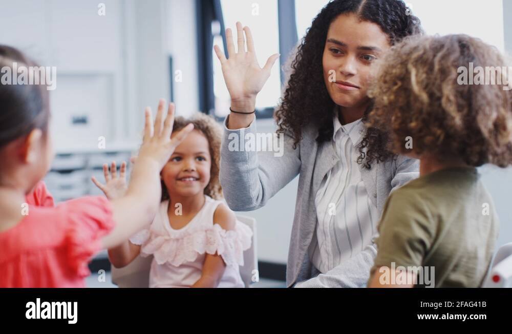 Infant school kids giving their teacher a high five in the classroom ...