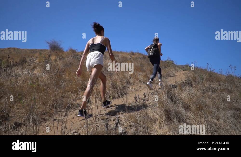 Two girls go uphill, one is in activewear, second is in shorts and top ...