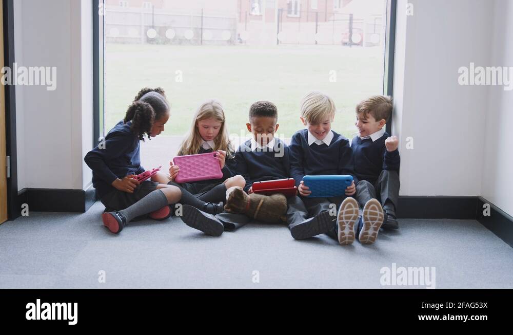 Five primary school kids sitting on the floor in a school corridor with ...