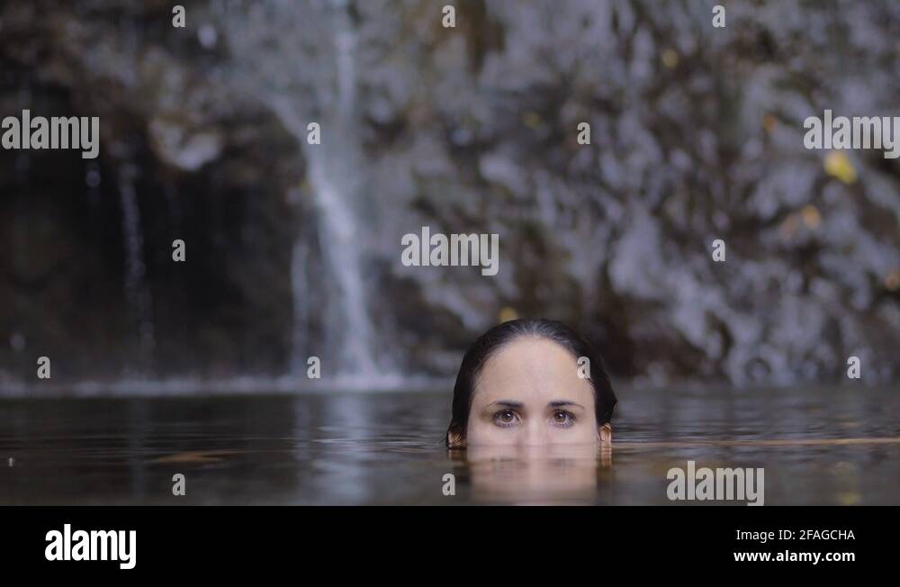 Beautiful mysterious woman swimming in waterfall, head half submerged ...