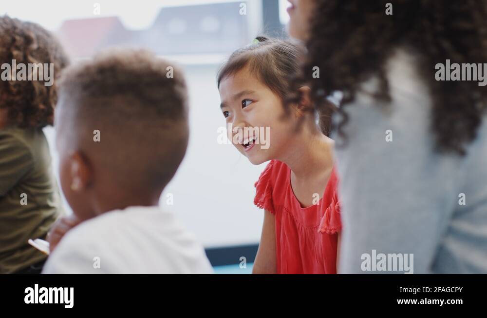 Infant school kids sitting on chairs in classroom talking to their ...