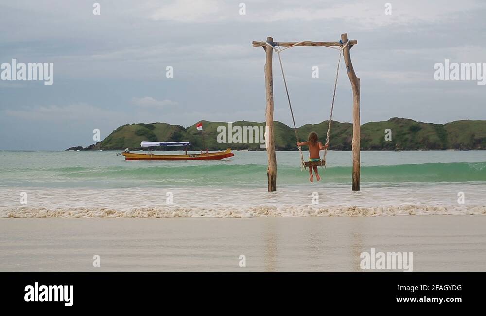 Back view of the girl having fun swinging at tropical island beach ...