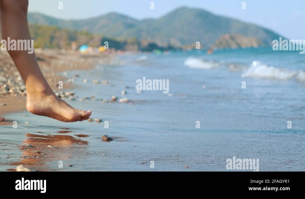 Girl touching sea water by foot. Female foot touching water wave at sea ...