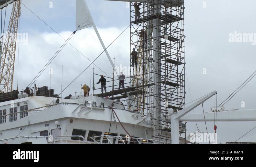 workers assemble scaffolding on ship mast in shipyard dry dock slow ...