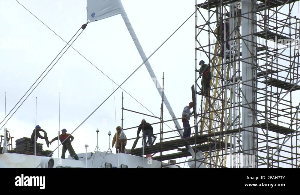 workers assemble scaffolding on ship mast in shipyard dry dock slow ...