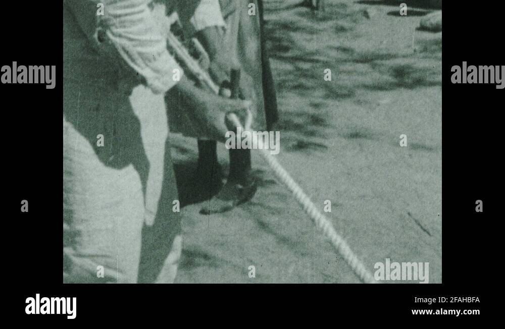 1930s: Man holding rope as it twists. Hands turning crank. Man turning ...