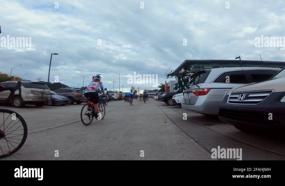 A group of cyclists ride through a parking lot filled with cars Stock ...