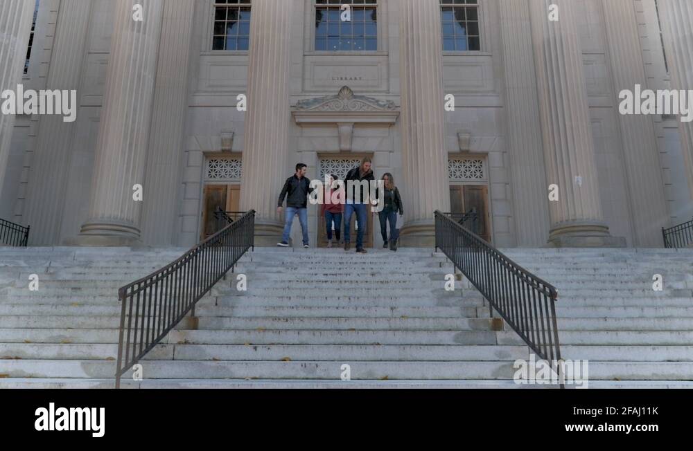 Four college university students walking down steps from a library ...
