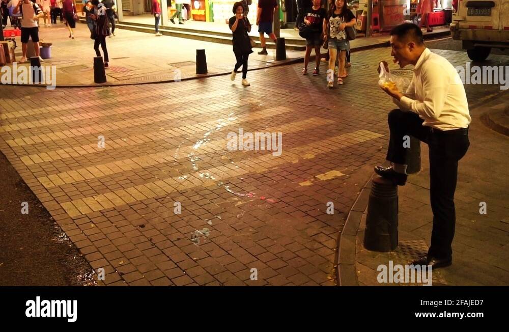 Man eating and pedestrians walking and standing on a busy side walk ...