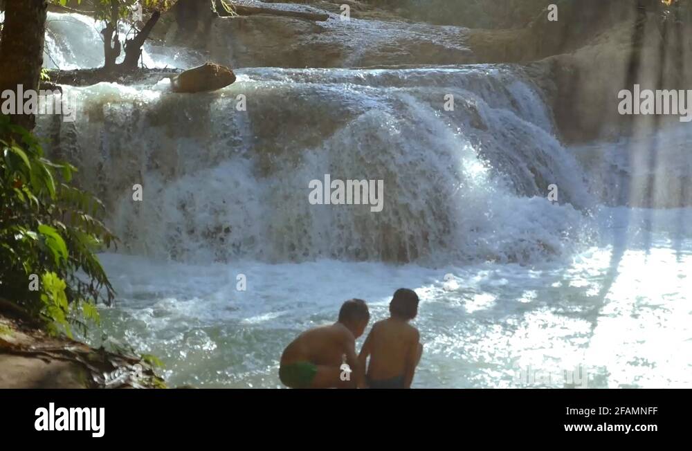 Two kids playing together next to a waterfall in Kuang Si waterfall in ...