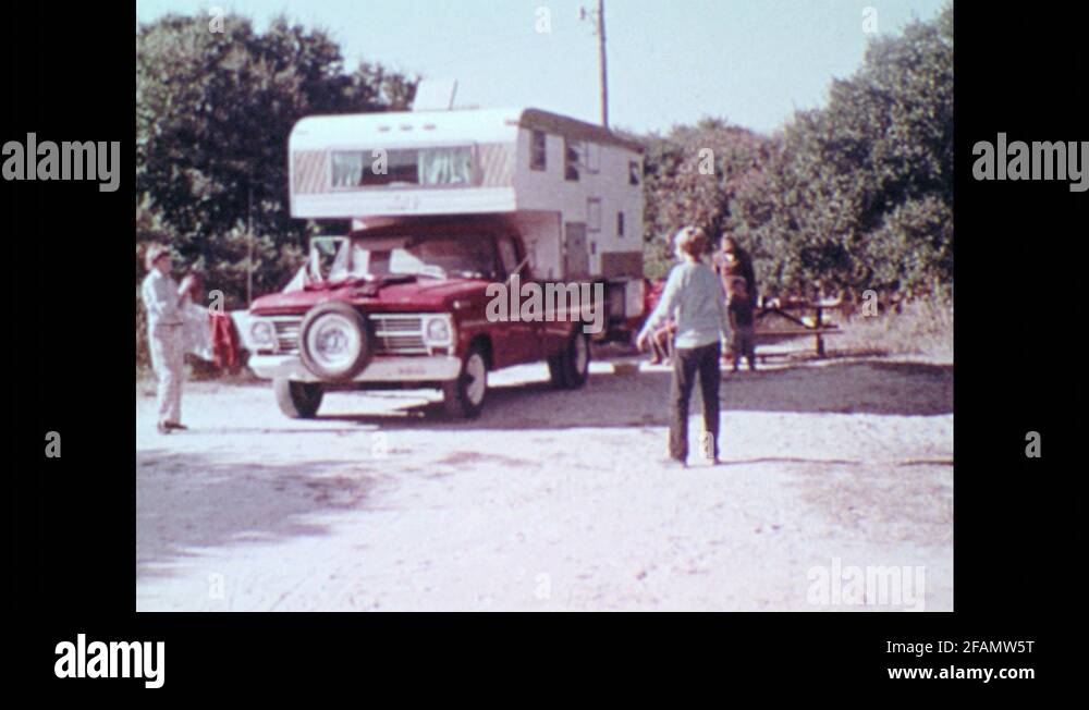 1970s: UNITED STATES: boys throw ball by camper van. Tree in park ...