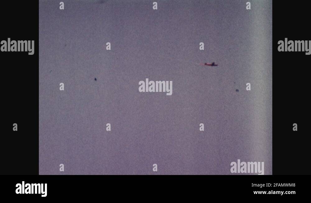 1970s: UNITED STATES: radio controlled plane in sky. Parachute opens on ...