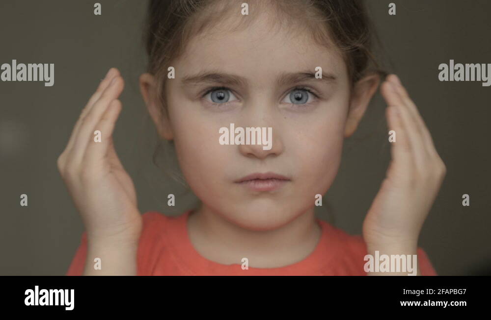 Cute little girl open her face with hands. Girl looks and is surprised ...