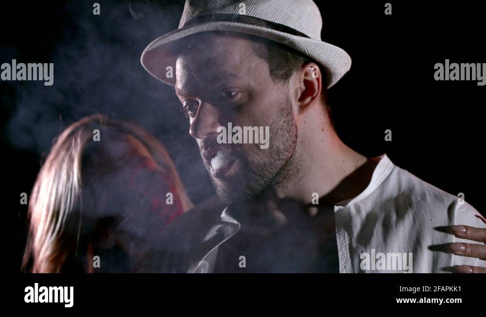 blonde woman is hugging muscular handsome man from back, he is smoking ...