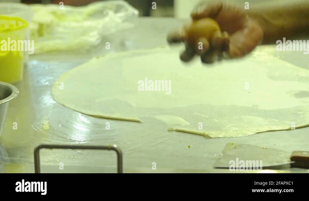 Indian man breaking an egg and pouring on the dough for roti canai at a ...