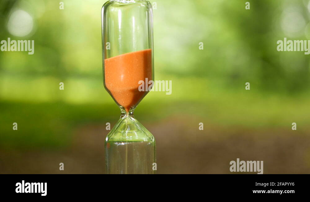 4K.Orange sand flows in glass hourglass , approach scene, green ...