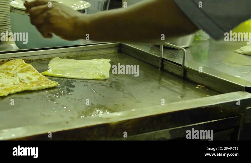 Indian man cooking roti canai on a griddle at a restaurant in Kuala ...