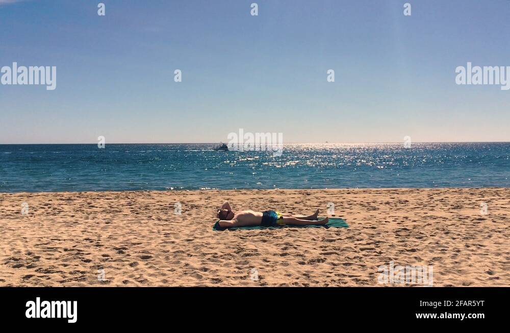Man Taking a Sunbath While a Boat Sails on the Horizon at Noon on a ...
