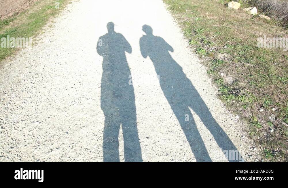 A silhouette shadow is cast onto a path as two friends walk together ...
