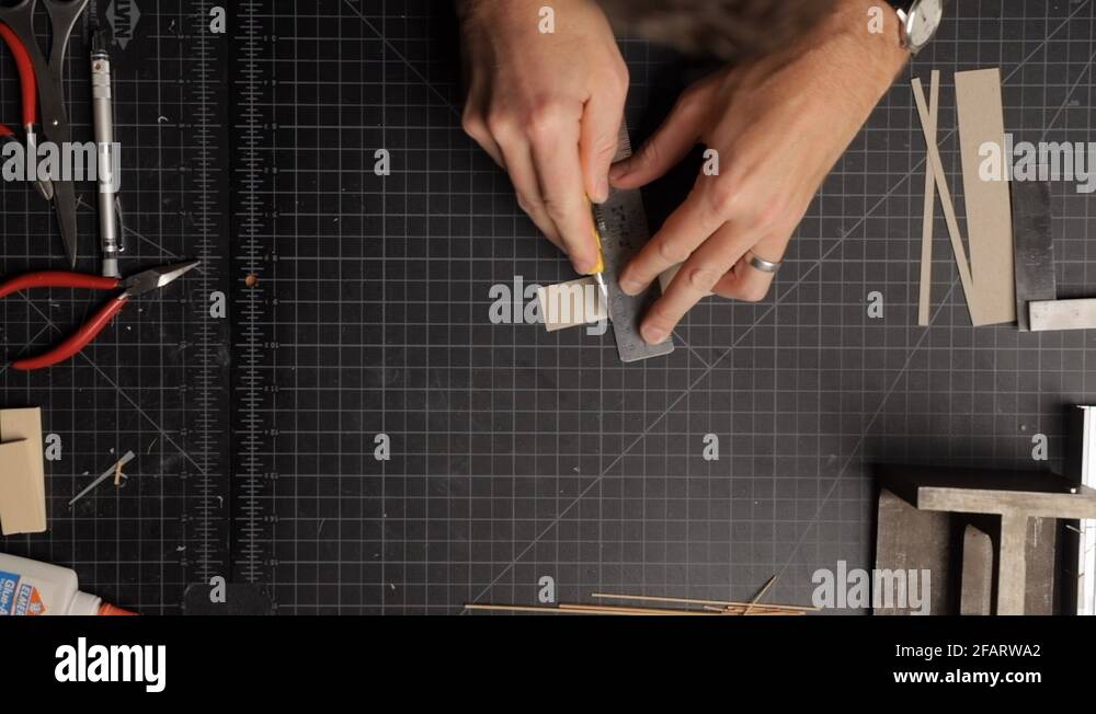 Overhead view of a male architect's hands scoring a strip of cardboard ...