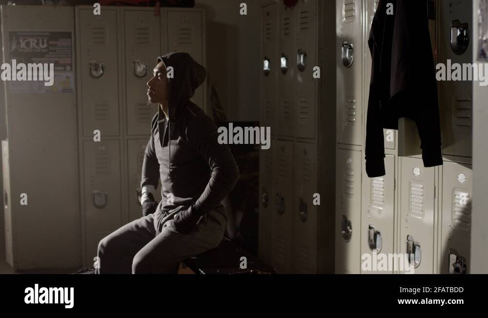 Boxer sitting on bench focused in musty locker room with hoodie on ...
