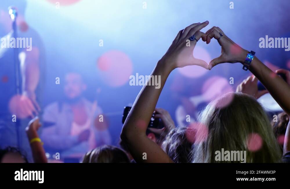 Girl doing heart with her hands to singer at concert with bubble ...