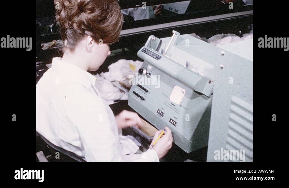 1960s: Woman seated at machine presses button and writes on sheet of ...