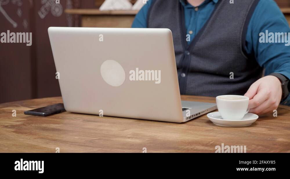 Male freelancer sips coffee while working from a small coffee shop ...