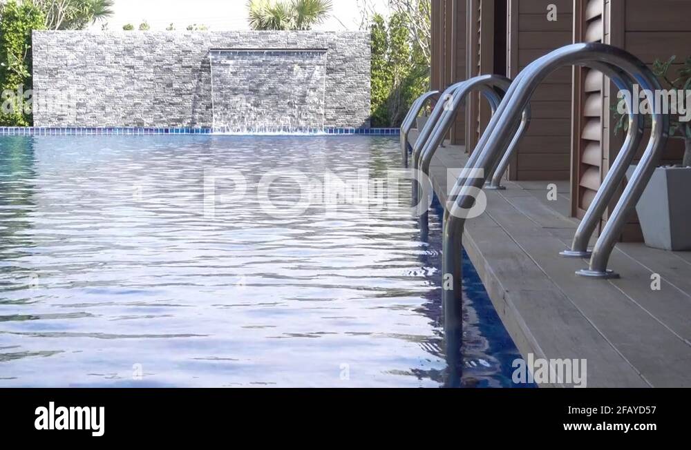 Swimming pool with metal stairs and wooden deck. Waterfall feature in ...