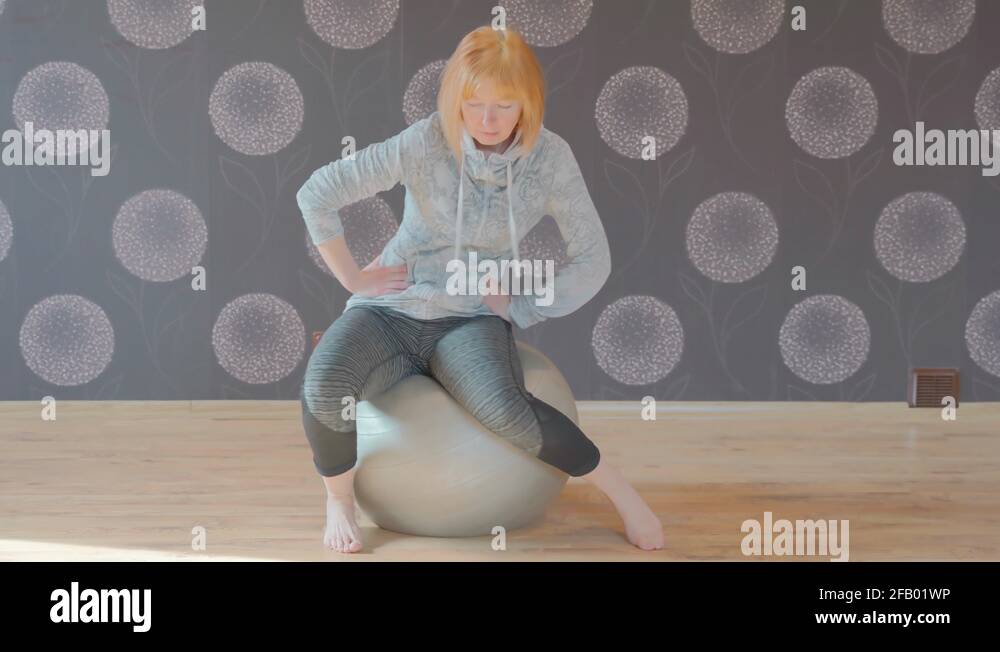 Well formed woman in her fifties doing workout indoors on a gym ball ...