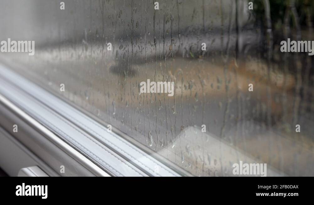 Static shot of slow rain hitting the lower part of a window frame seen ...