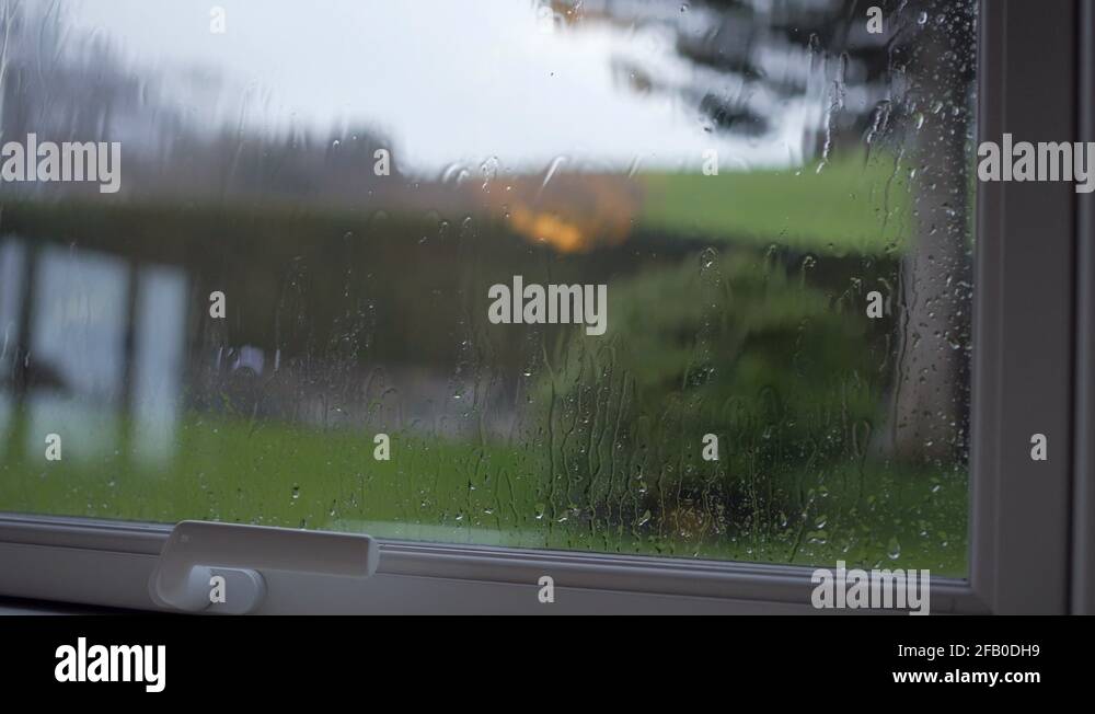 Static shot of rain hitting a window seen from inside a house looking ...