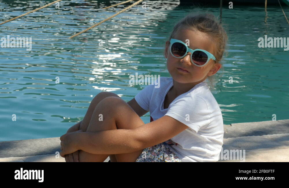 Little girl, kid sits on dock at seaport and looks around and dreaming ...