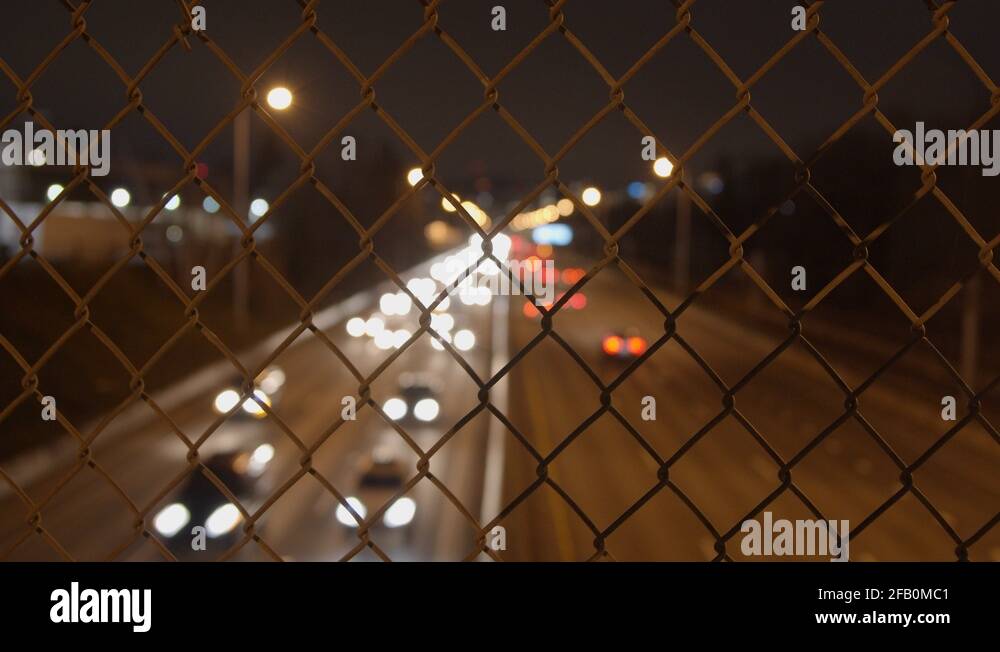 Night view along highway from overpass, looking through chain link ...