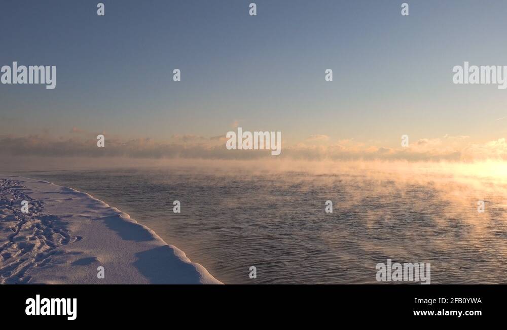 steam rising from a very cold lake as the morning sun rays shine on the ...
