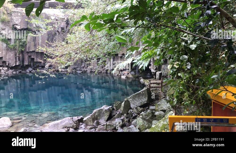 A shallow blue colored pool at Cheonjiyeon Waterfalls in Jeju Island ...