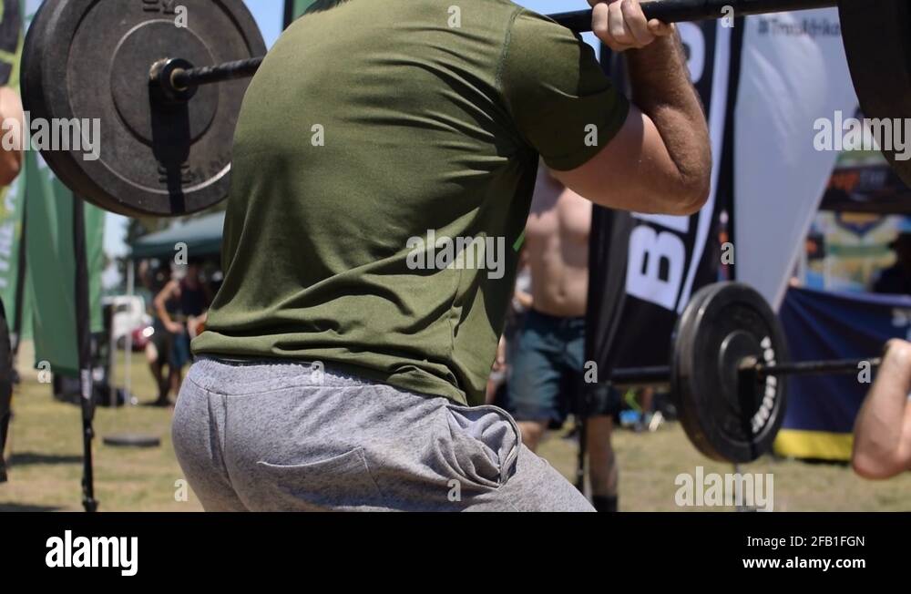 A fit bearded man squatting using an olympic barbell during a cross fit ...