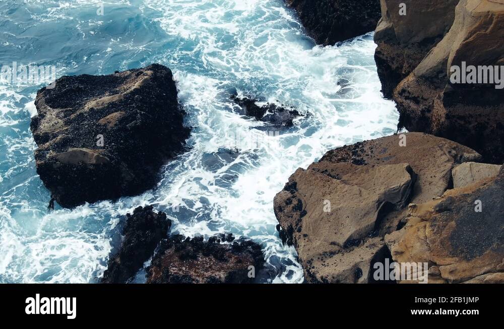 weather blackened jagged cut orange sandstone cliff overhangs deep teal ...