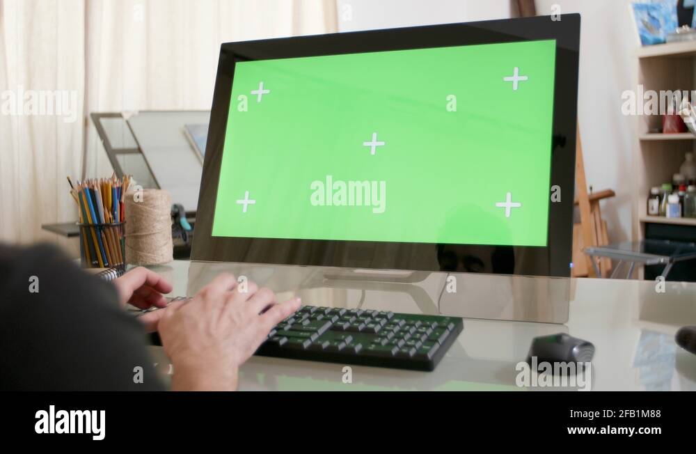 Man typing a text on his keyboard with a green screen on his monitor ...