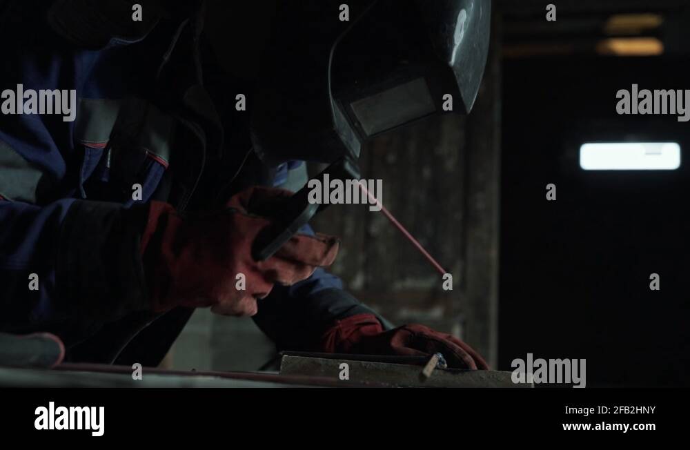 Slow-motion, side view welder in welding mask welds two metal parts ...