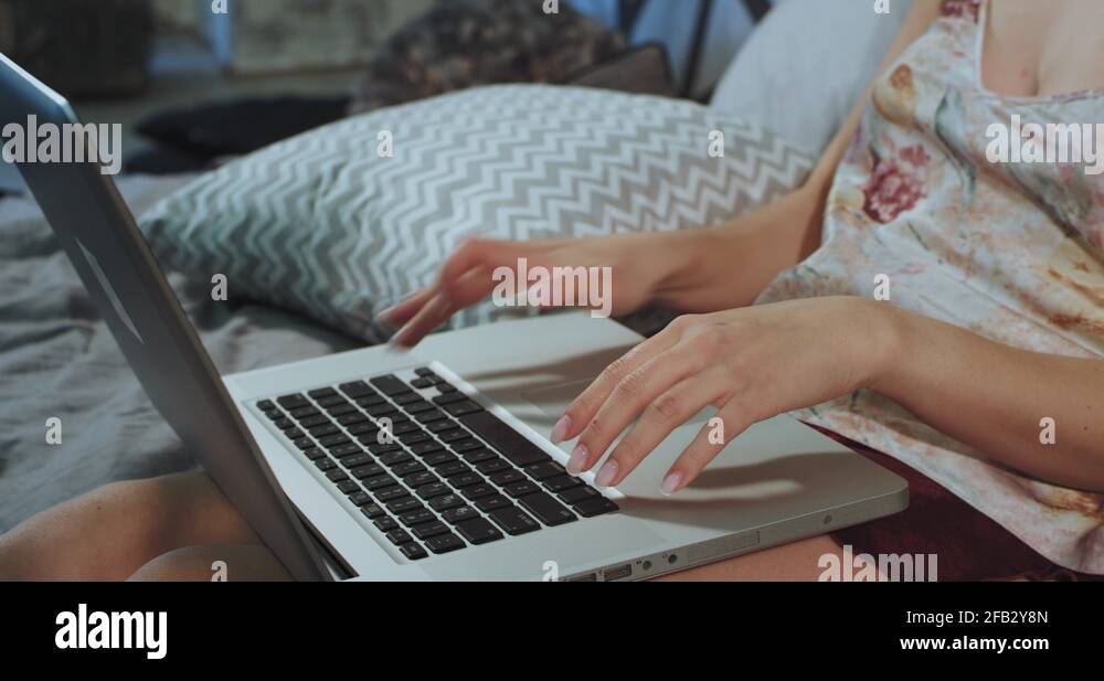 Typing lady on the notebook in pajamas , laying down on the bed and ...
