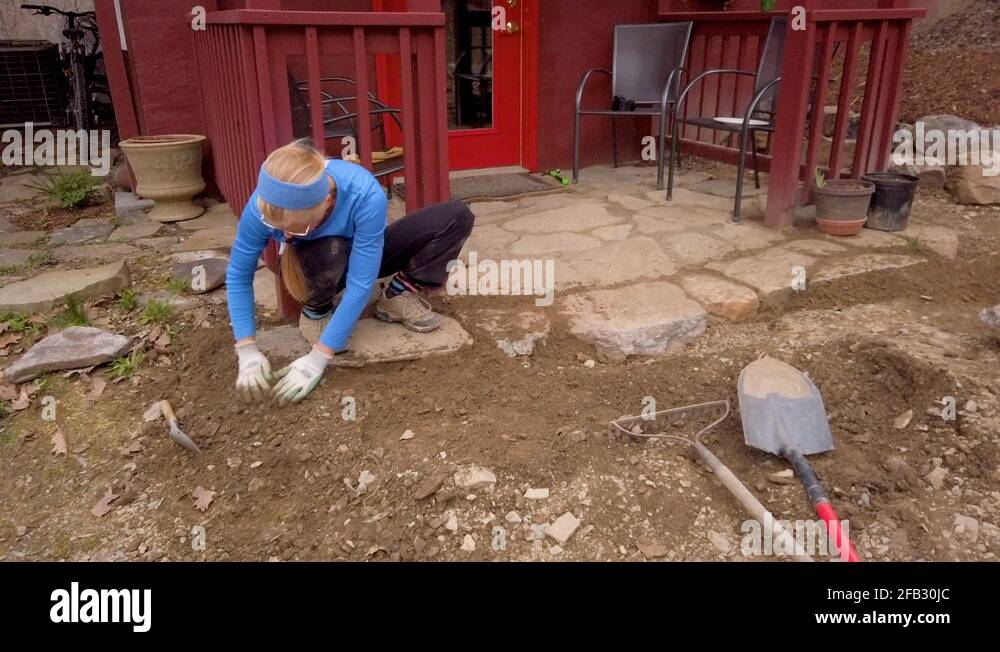 Woman with trowel pressing dirt under rock to set large stone paver ...