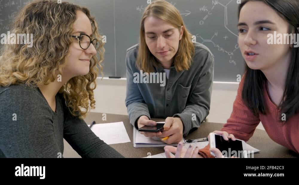 Three students having a discussion while holding mobile phones in a ...