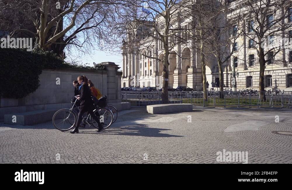 Bicycle riders pushing their bikes past the German Reichstag building ...
