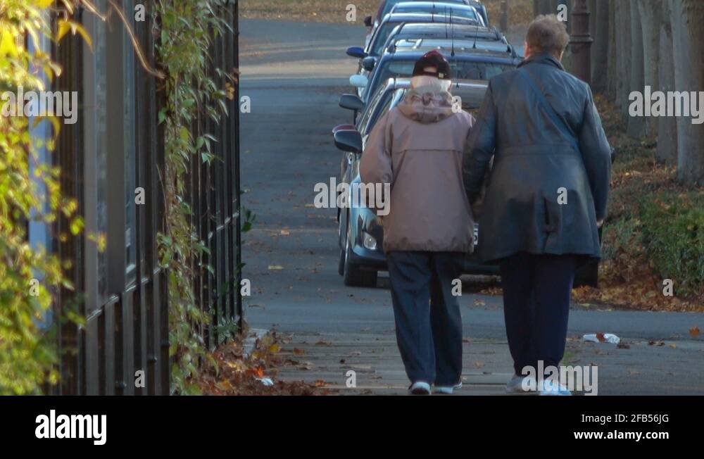 An elderly couple walking away and around a corner while holding hands ...