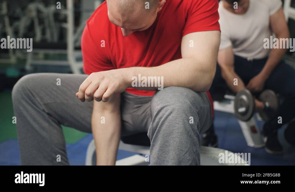 In the gym man sits and lifts a dumbbell with one hand. Young ...