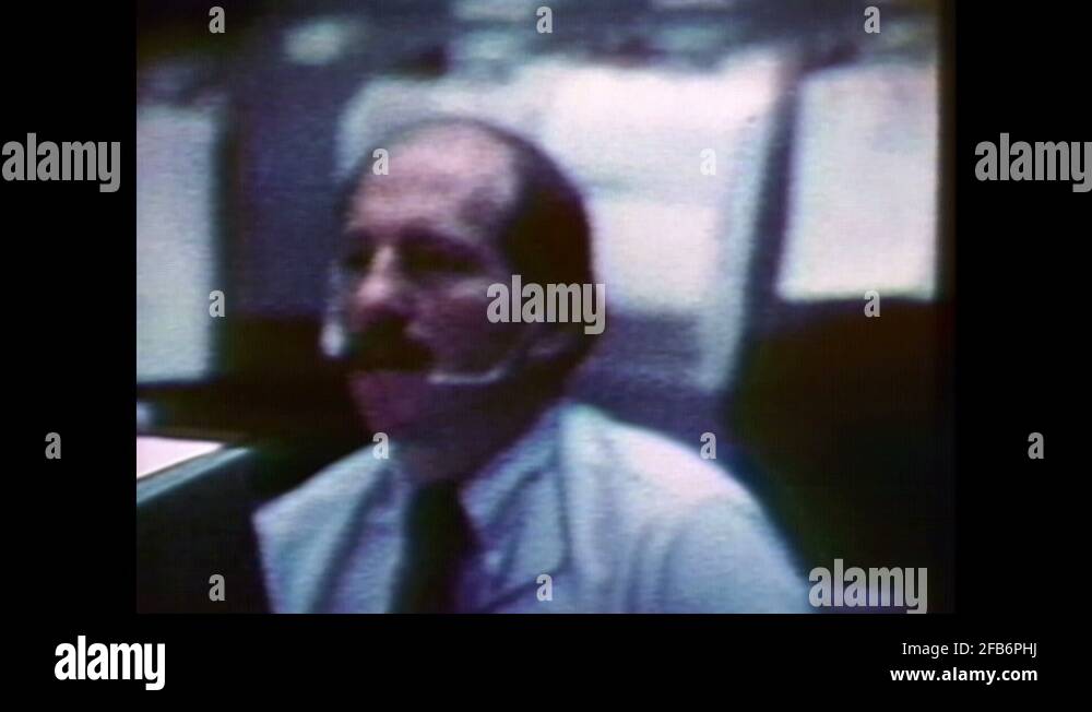 1980s: Mission control room. Man speaks. Map. Sign reads "WELCOME HOME ...