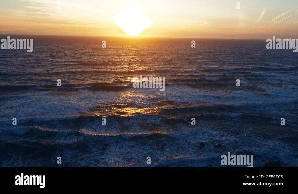 Drone captures a setting sun at golden hour over empty a rocky beach ...