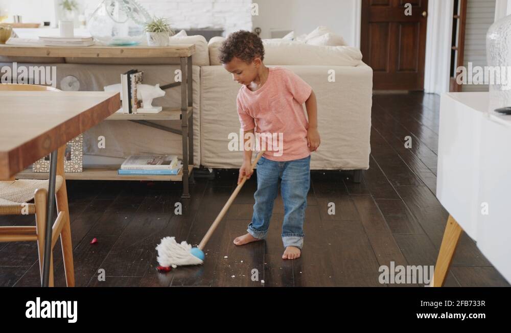 Three year old African American boy cleaning dining room floor with a ...