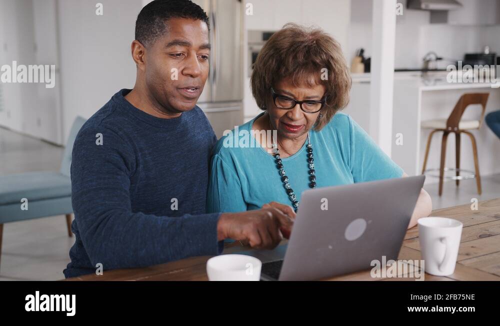Middle aged black man helping his mother use a laptop computer at home ...